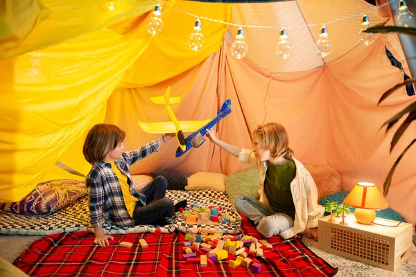 Two best buddies are playing in an indoor blanket tent with airplanes ...