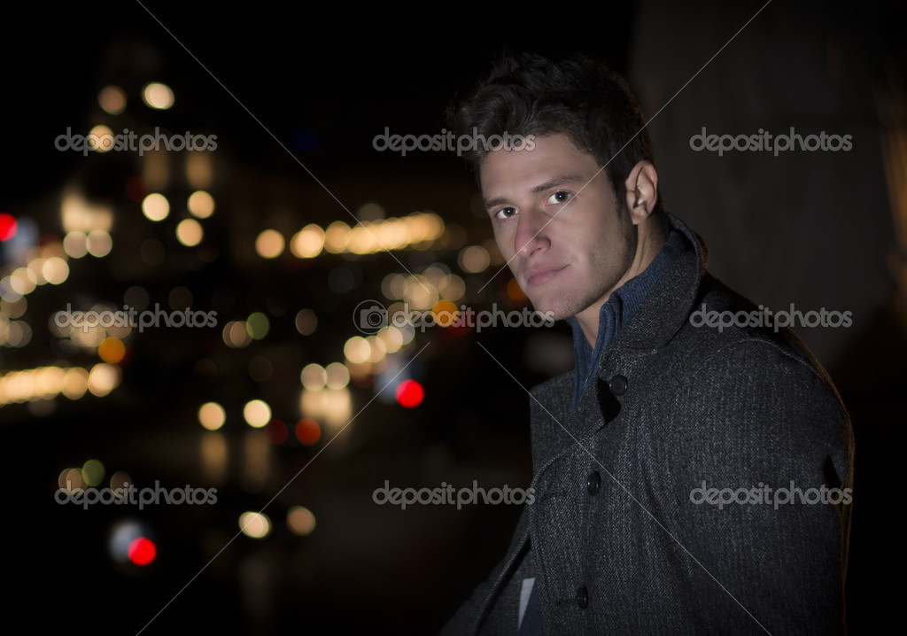 Attractive young man portrait at night with city lights behind him ...