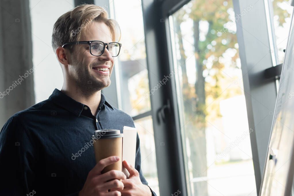 Programador feliz con café para llevar y carpeta de papel de pie cerca ...