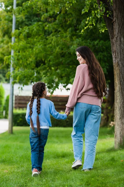 back view of mother and daughter in jeans holding hands while walking ...
