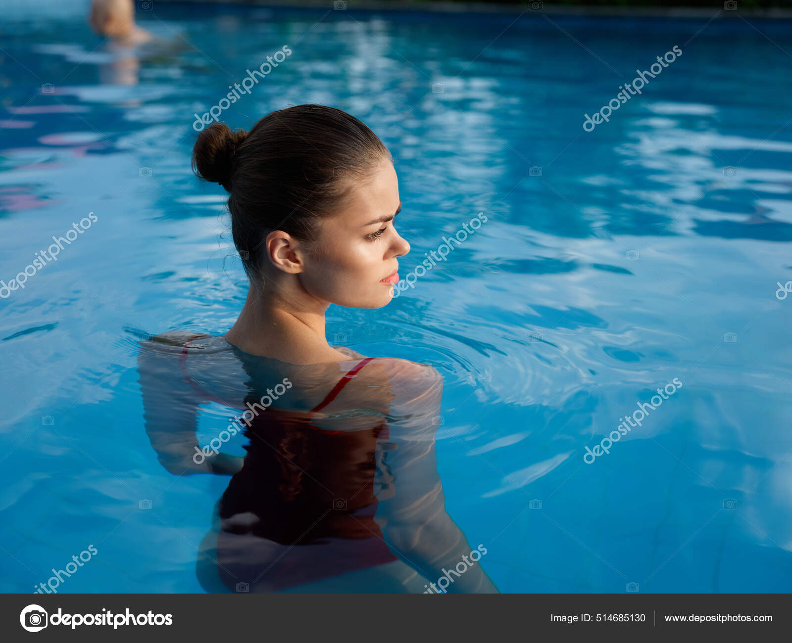 Pretty woman with bare shoulders in a swimsuit stands in the pool back ...