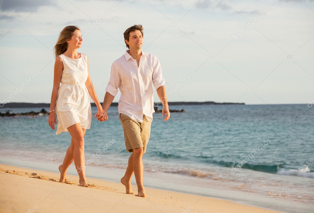 Romántica pareja feliz caminando en la playa al atardecer. Aguantamiento sonriente 2023