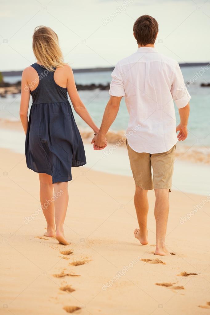Romántica pareja feliz caminando en la playa al atardecer. Aguantamiento sonriente 2023