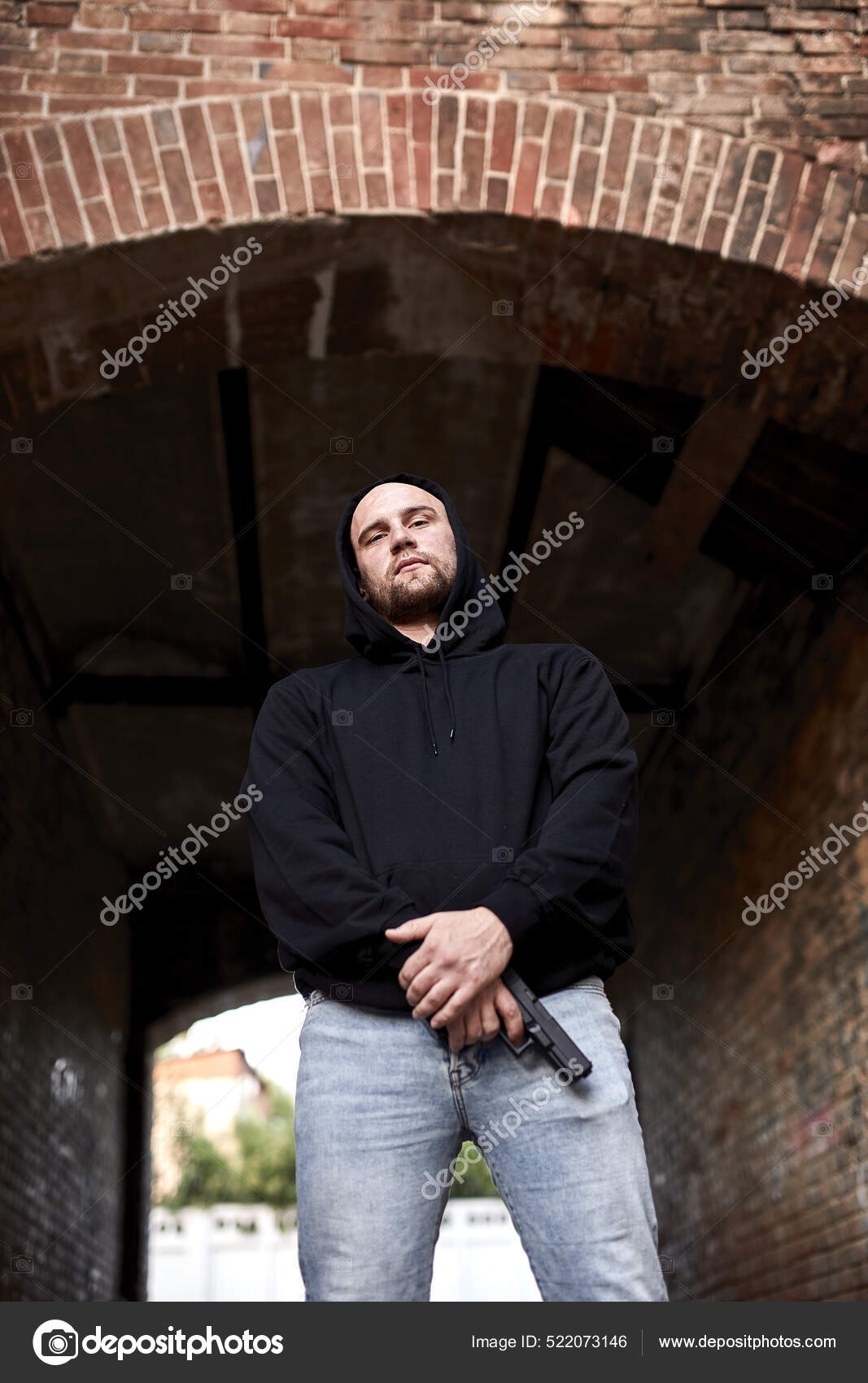 Aggressive Hooligan man in the hood with gun standing at street alley ...