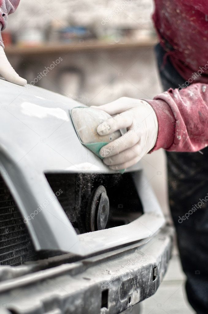 Mechanic prepairing the body of a car for a paint job by appling the ...
