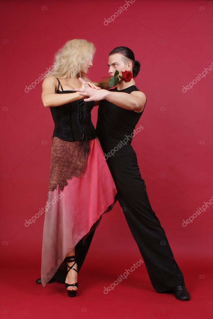 Beautiful blond and brunet with rose in teeth dancing tango on red ...