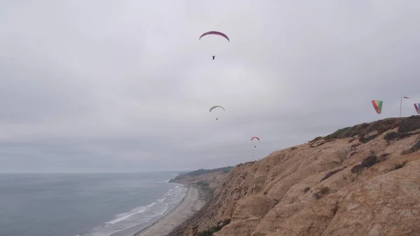People paragliding, Torrey Pines cliff or bluff. Paraglider soaring in ...