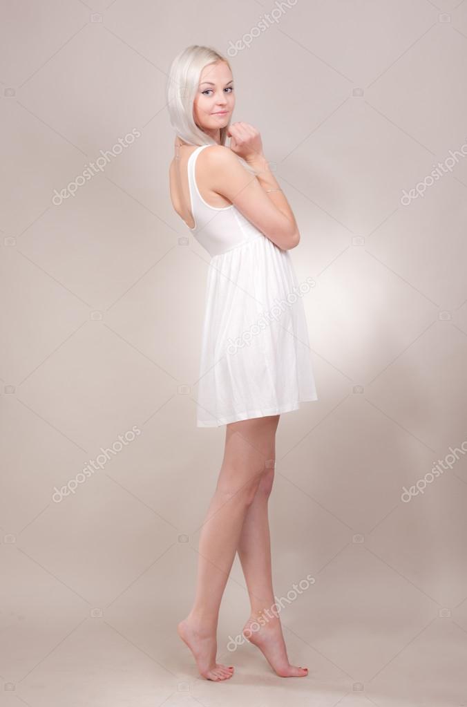 Beautiful barefoot girl in a short white dress on a gray background ...