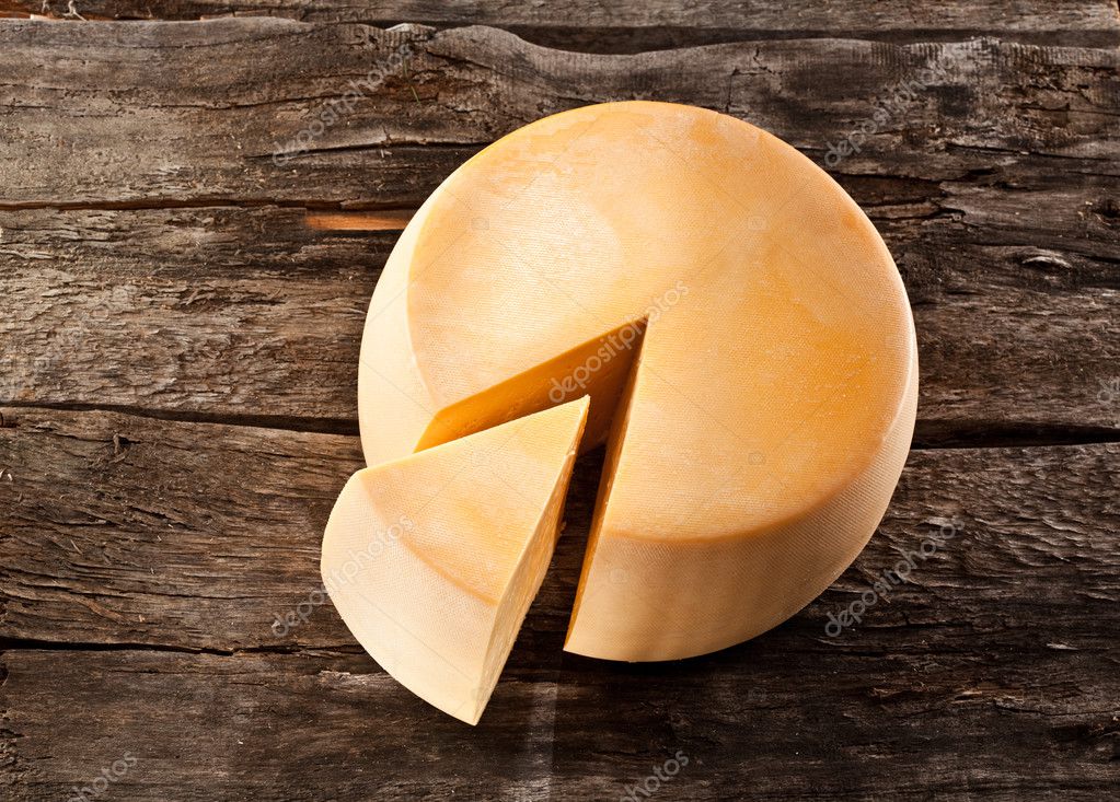 Cheese wheel on wooden table Stock Photo by ©utima 40812197