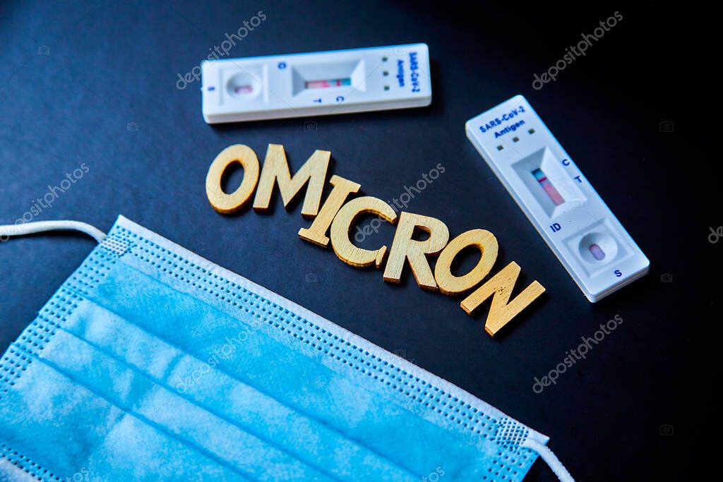 omicrón palabra hecha de letras de madera, máscara médica azul y 2 autopruebas de antígeno covid ...