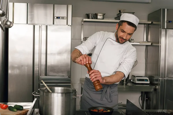 Chef adding salt or pepper to dish while cooking on restaurant kitchen ...