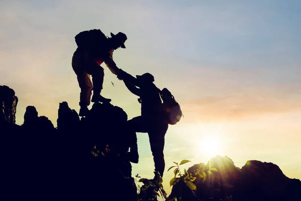 Silhouette climbing buddies help each other climb up the mountain at ...