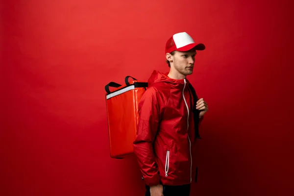 Delivery man in a red jacket and cap carry red thermal backpack full of ...