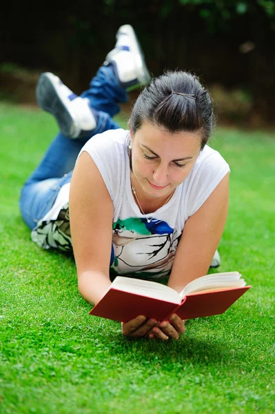 Young beautiful woman lays on green field and reads book. - Stock Image ...