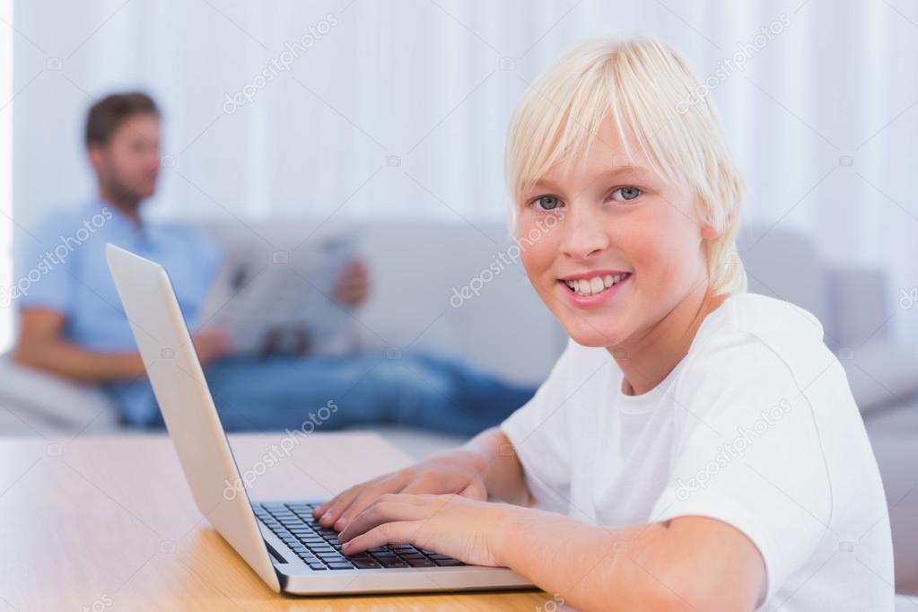 Little boy using laptop while his father is reading on the couch ...