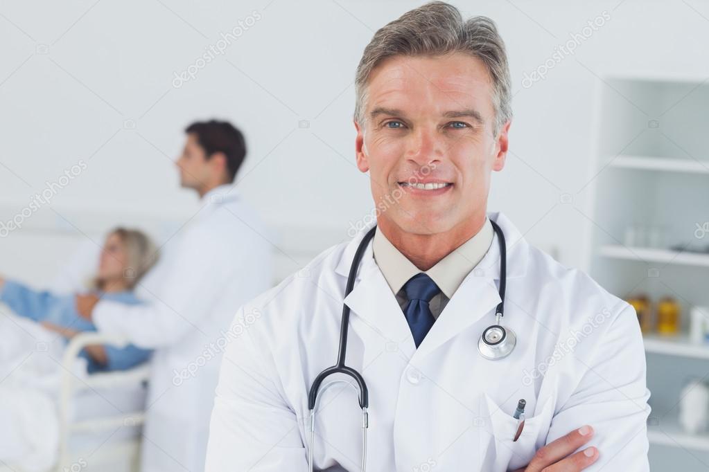 Experienced doctor posing with doctor attending patient on backg Stock ...
