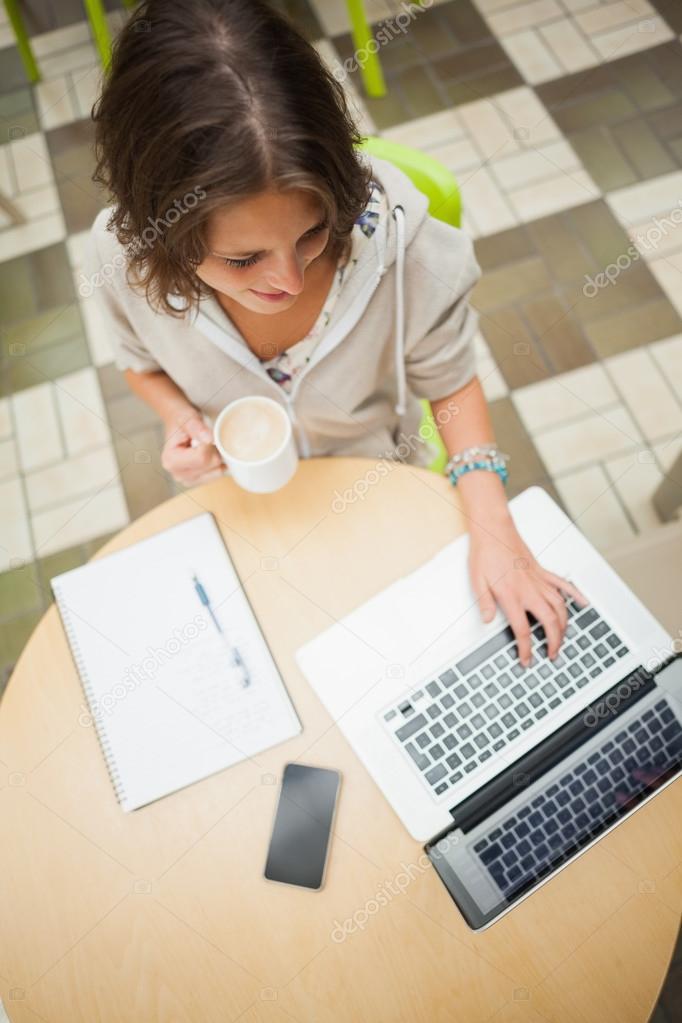 Student drinking coffee while using laptop at cafeteria table Stock ...