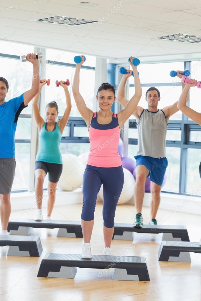 Instructor with fitness class performing step aerobics exercise with ...