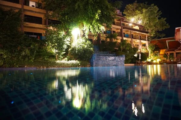 Night pool with lighting and green trees. Smooth water is like a mirror ...
