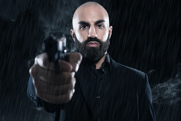 Dangerous bald gangster man with beard holding gun. Wearing blac Stock ...