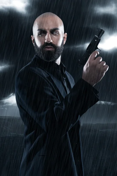 Dangerous bald gangster man with beard holding gun. Wearing blac Stock ...