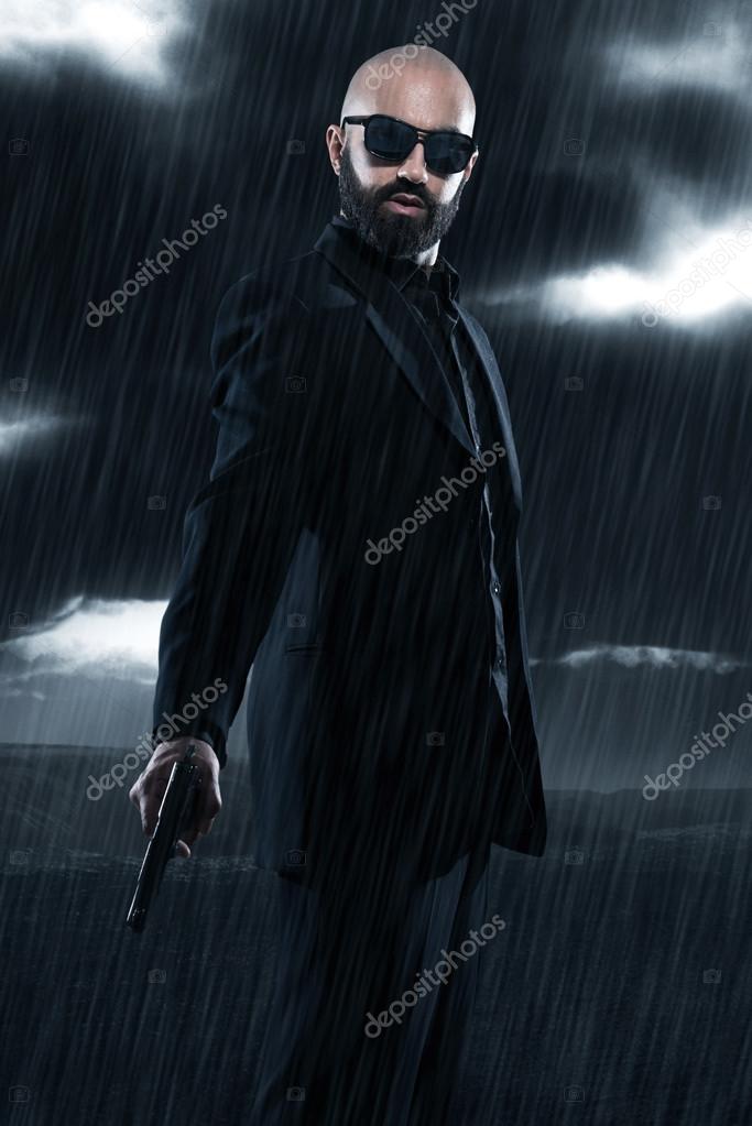 Dangerous bald gangster man with beard holding gun. Wearing blac Stock ...