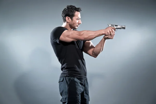 Action hero muscled man shooting with gun. Wearing black t-shirt ...