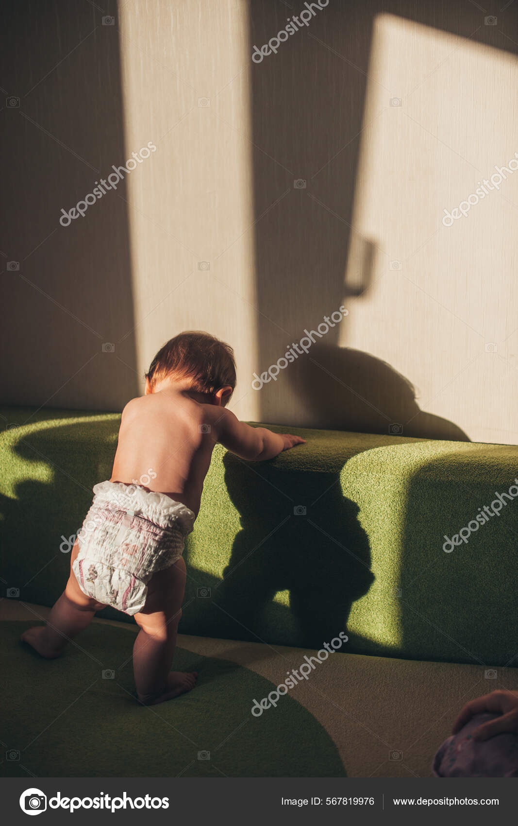 Back view baby girl standing on a sofa in the living room only in a ...
