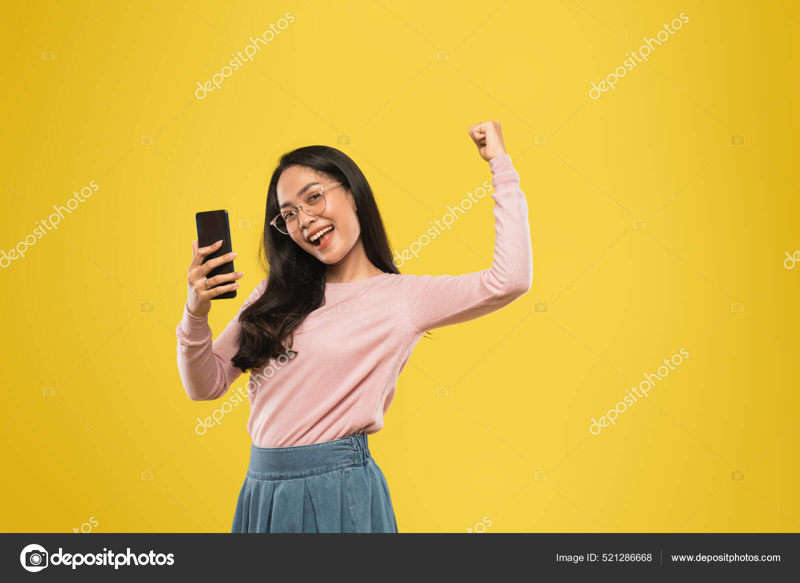 Woman in glasses smiling with one hand raised while using a smartphone ...