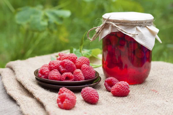 Raspberry preserve in glass jar and fresh raspberries on a plate ...