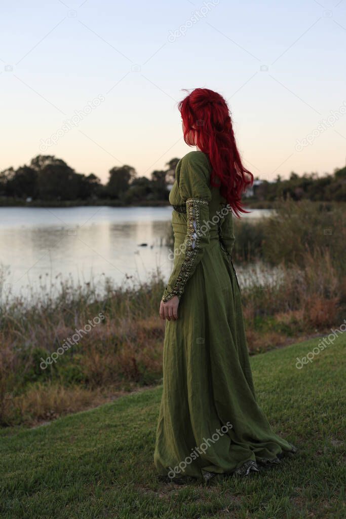 Retrato de cuerpo entero de mujer pelirroja con un hermoso vestido de fantasía medieval verde ...