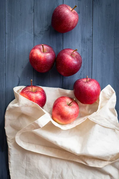 Red apples in white fabric reusable bag placed on wooden table. Eco ...