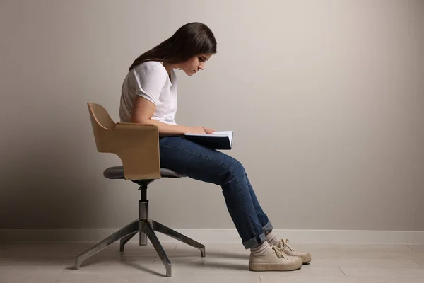 Young woman with bad posture reading book while sitting on chair near ...