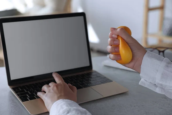 Woman squeezing antistress ball while working on laptop in office ...