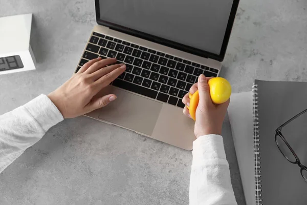 Woman squeezing antistress ball while working on laptop at table, above ...