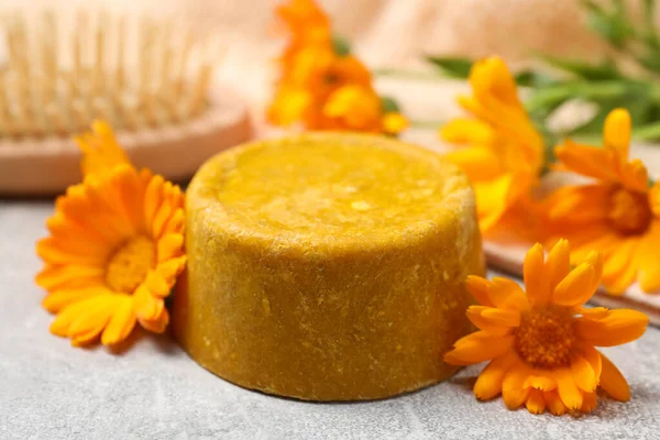 Yellow solid shampoo bar and flowers on light table, closeup. Hair care ...