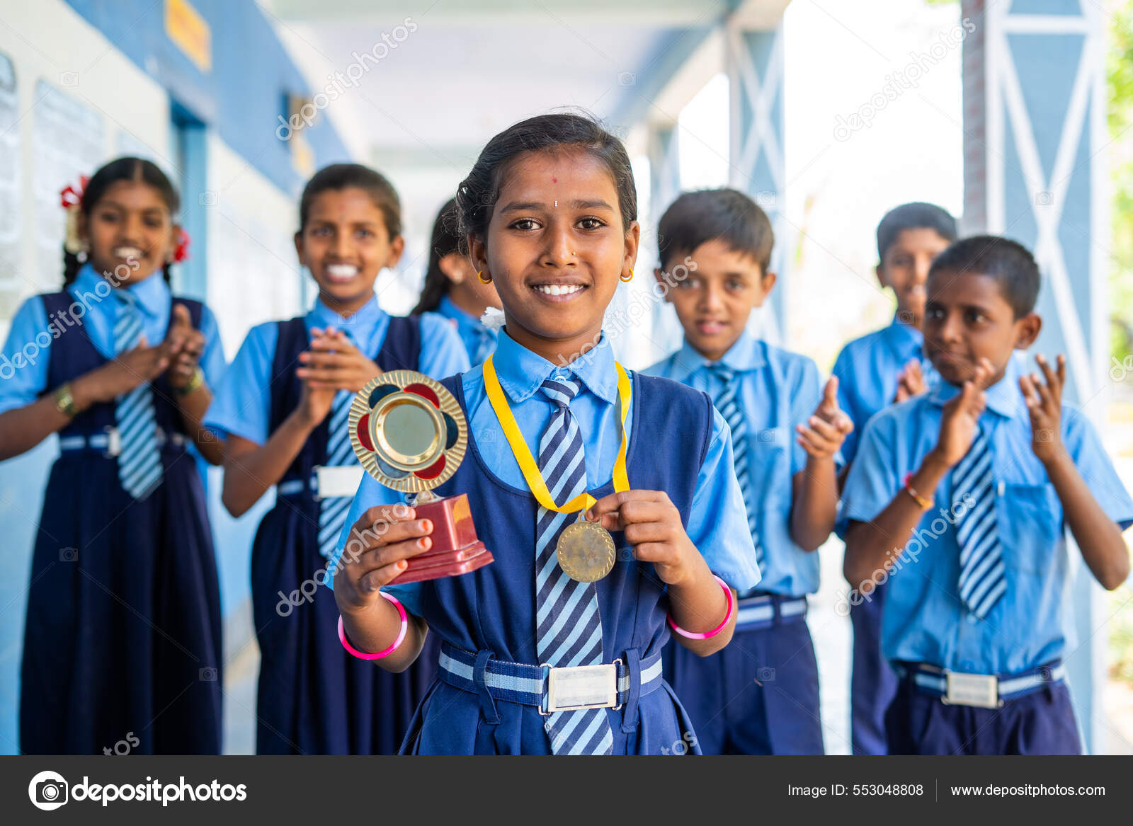 Proud girl with winner trophy and medal with cheeful students ...