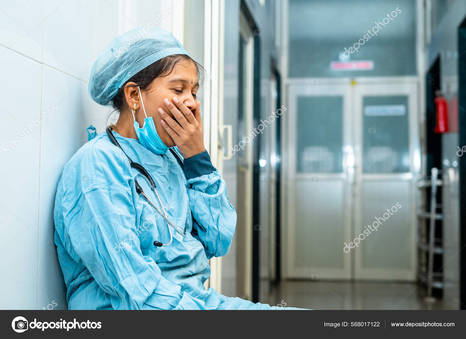 Yawning surgeon while sitting at hospital corridor after surgery near ...