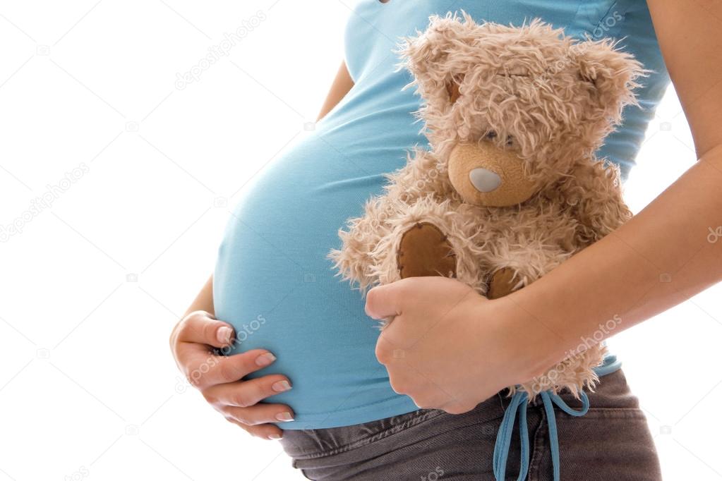 Una mujer embarazada con un oso de peluche sobre un fondo blanco ...