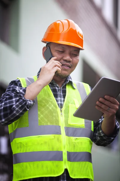 Portrait of construction worker wearing safety vest talking on t ...