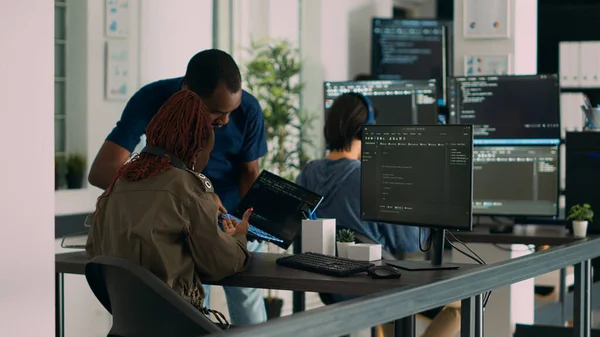 Database developer explaining algorithm to colleague coder pointing at running code on laptop ...