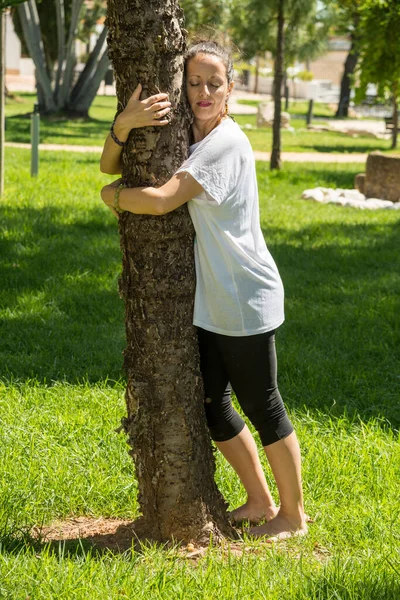A woman sunbathes standing and hugging a tree. Hugging a tree has many ...