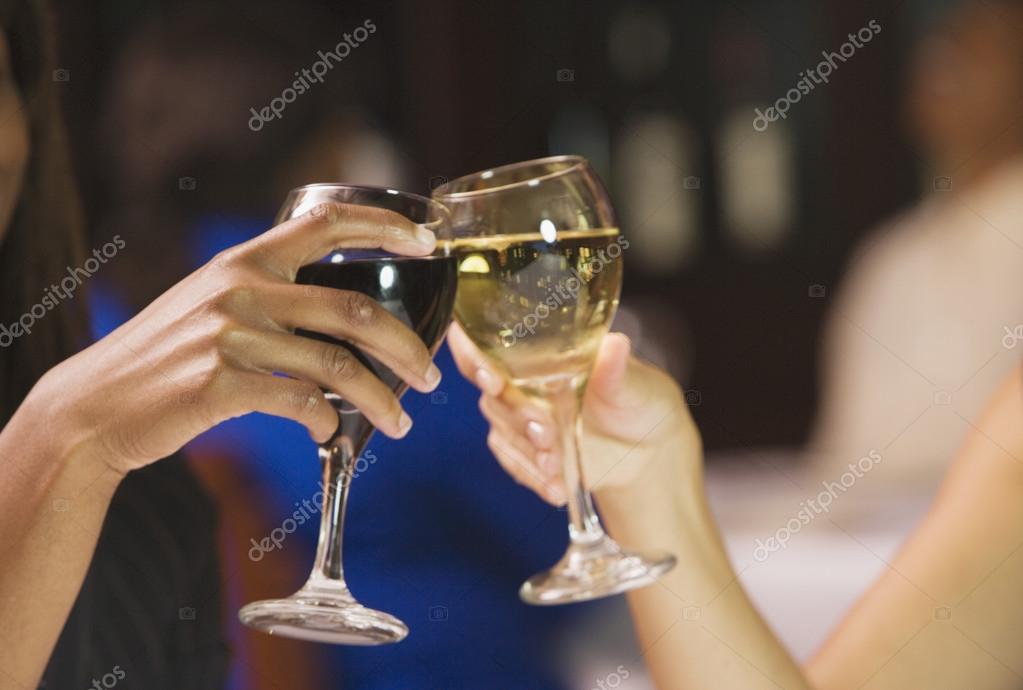 Cerca de las manos de dos de las mujeres brindando con copas de vino ...