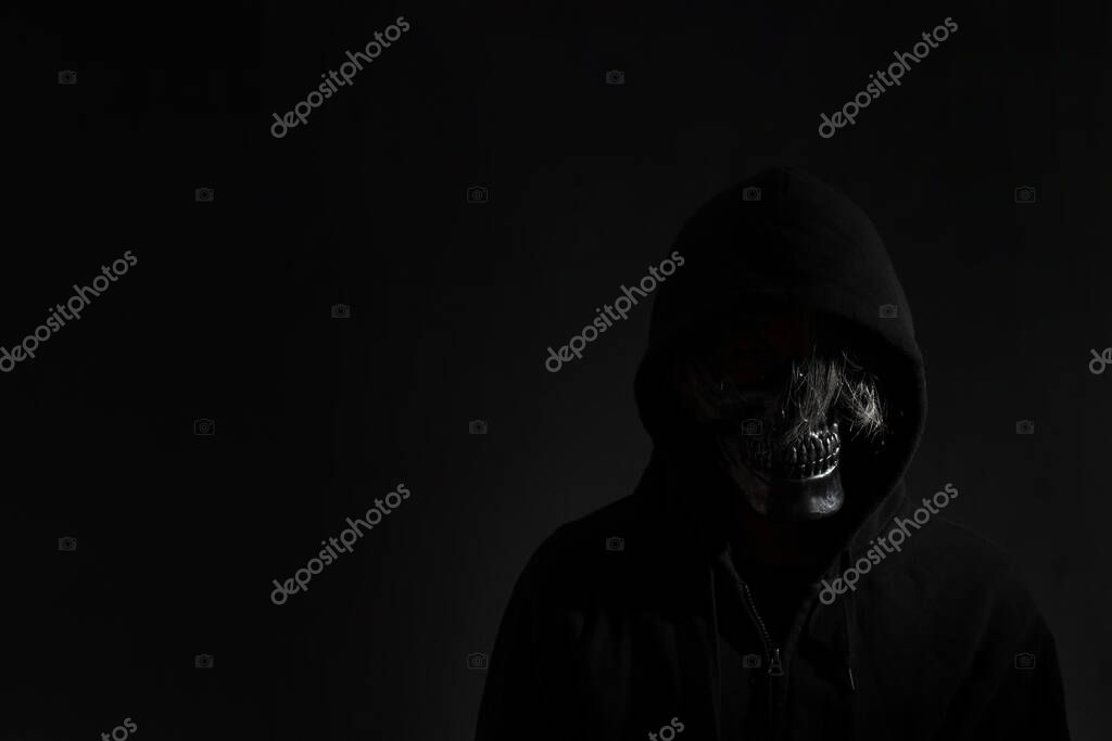 El hombre de horror con máscara de cráneo de pie en la oscuridad. 2022