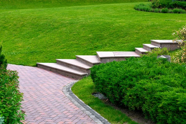 Granite steps to path from brick stone tile in a park on a slope with ...