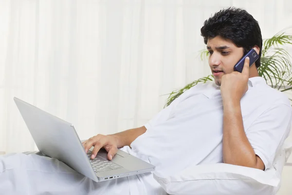Young man using cell phone while working on laptop - Stock Image ...