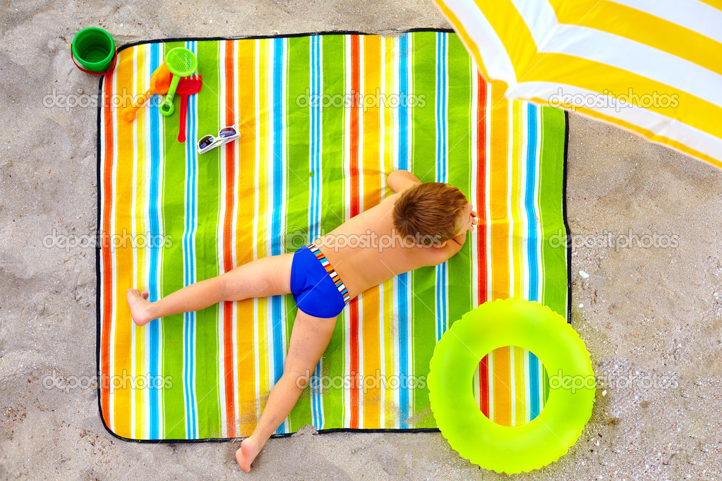 Cute kid sunbathing on colorful beach Stock Photo by ©olesiabilkei 31601475
