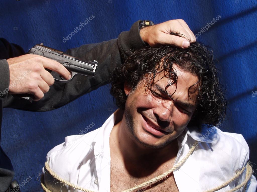 Desperate kidnapped man sitting in the room with the oversight of a gun ...