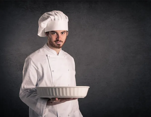 Young cook man with uniform showing baking tin over grunge background ...