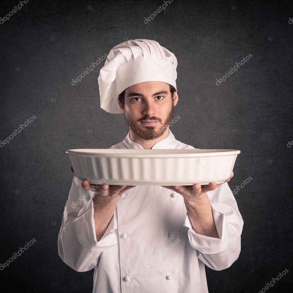 Young cook man with uniform showing baking tin over grunge background ...